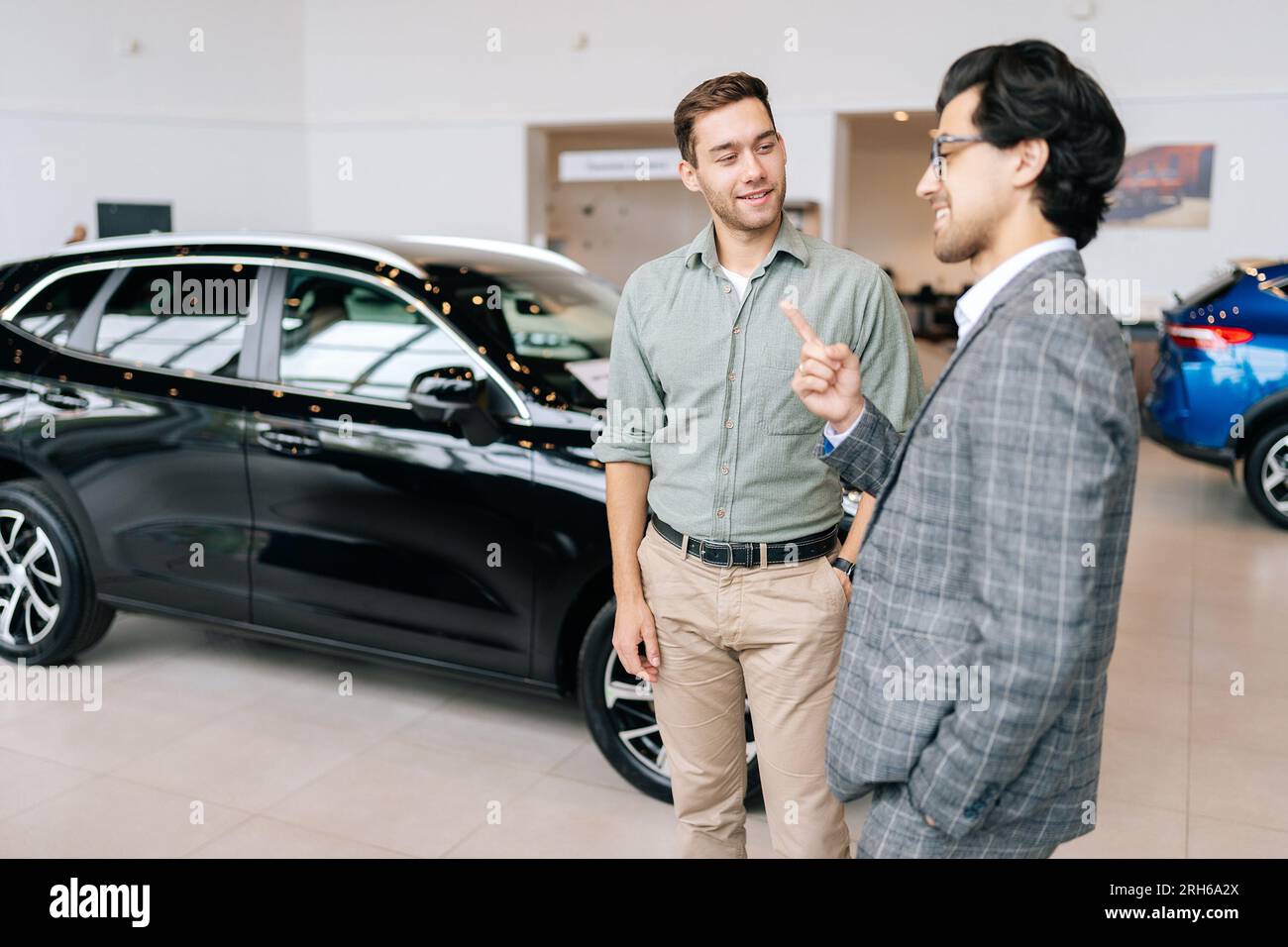 Side view of friendly male car seller with bearded male customer in in ...