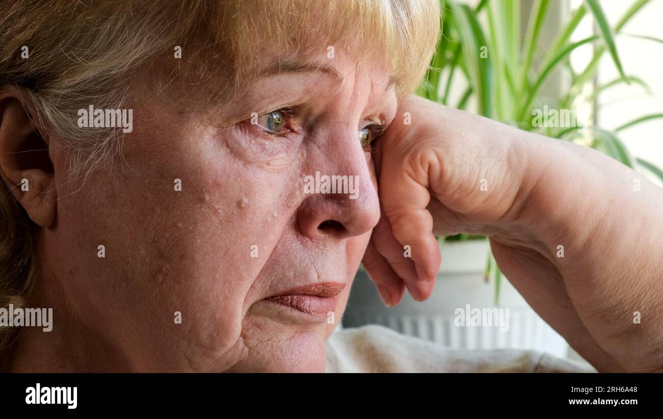 Old woman crying at the window. Face of depressed elderly woman at home ...