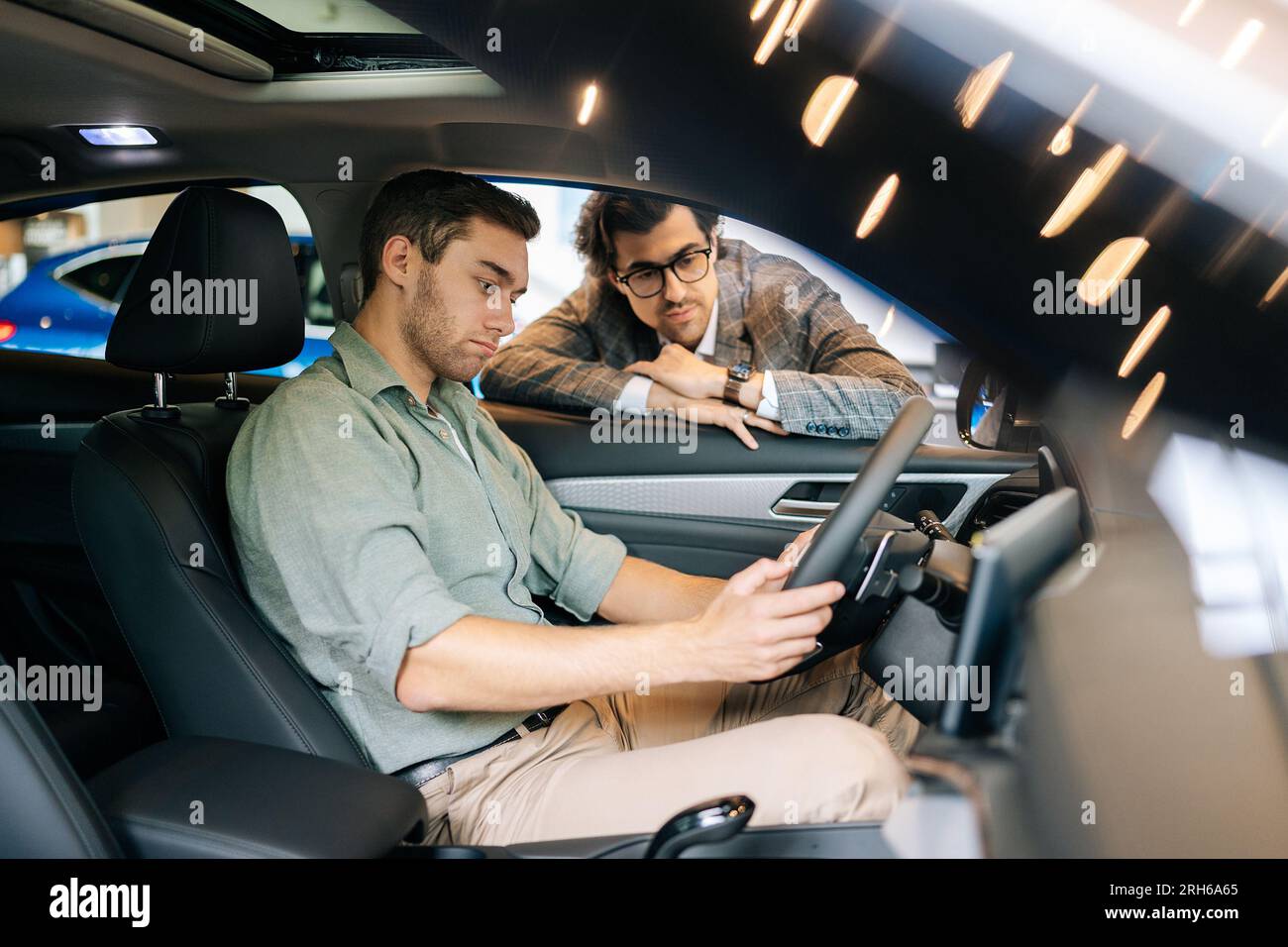 Side view of pensive male customer sitting on front seat of new car in ...