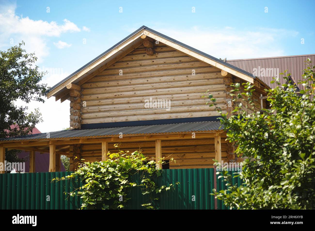 An under construction wooden house with a grey roof behind a green ...