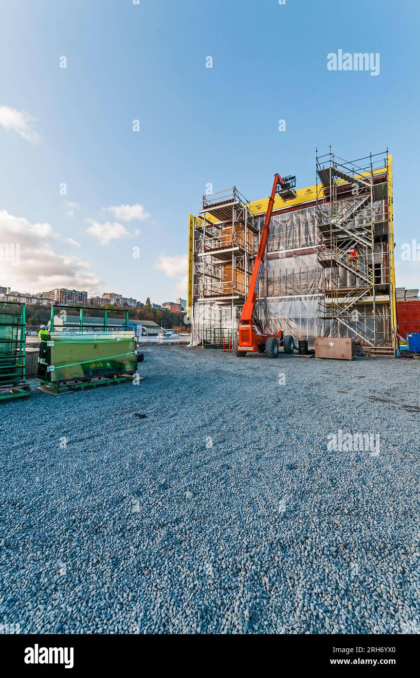 An orange rental high-lift with its arm extended to roof of building at ...