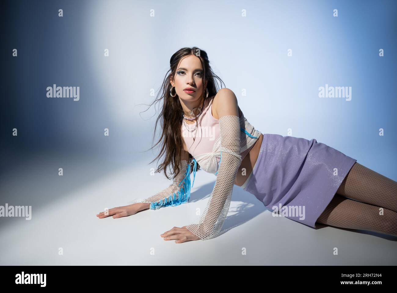 Trendy young asian woman in mesh top and skirt looking at camera while ...