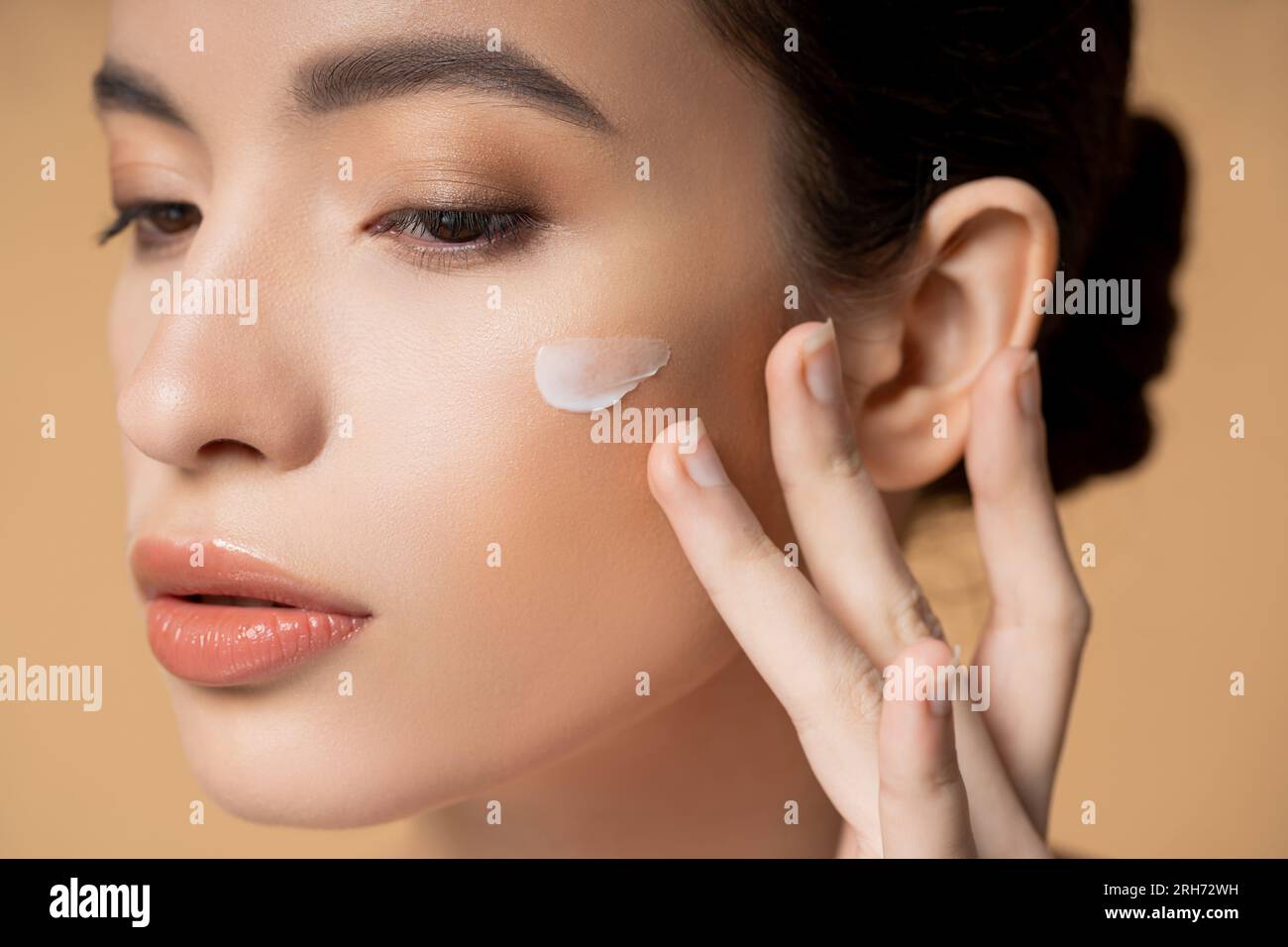Close up view of young asian woman applying face cream on cheek ...