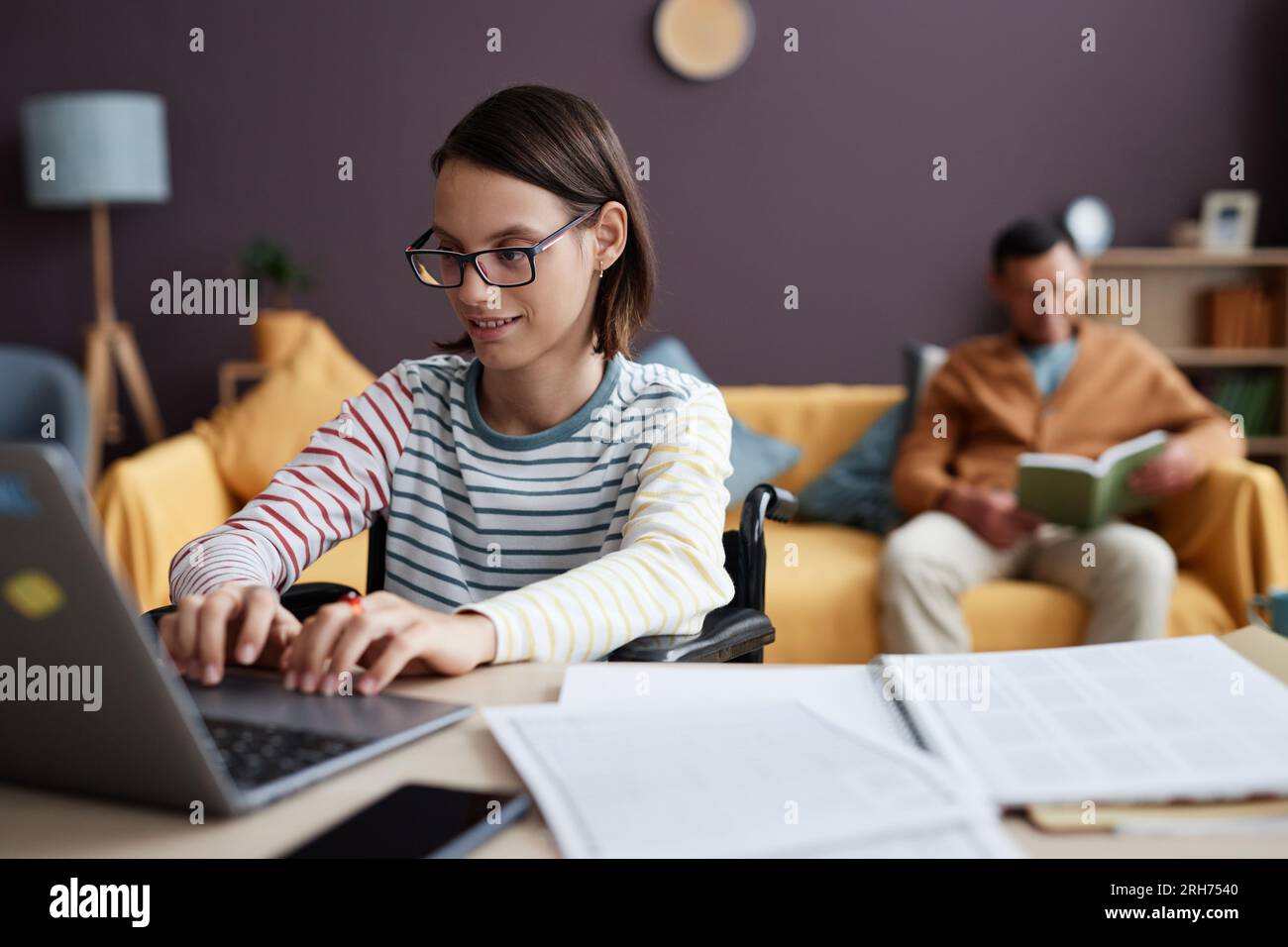 Portrait of smiling teenage girl with disability using computer at home ...