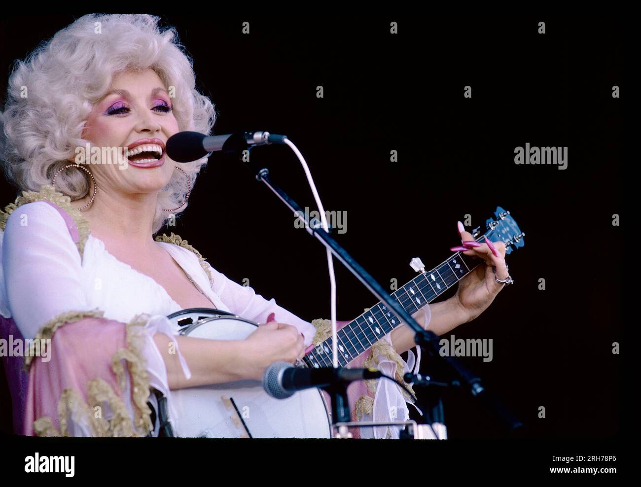 A beaming smiling Dolly Parton plays a 5 string banjo in spite of her ...
