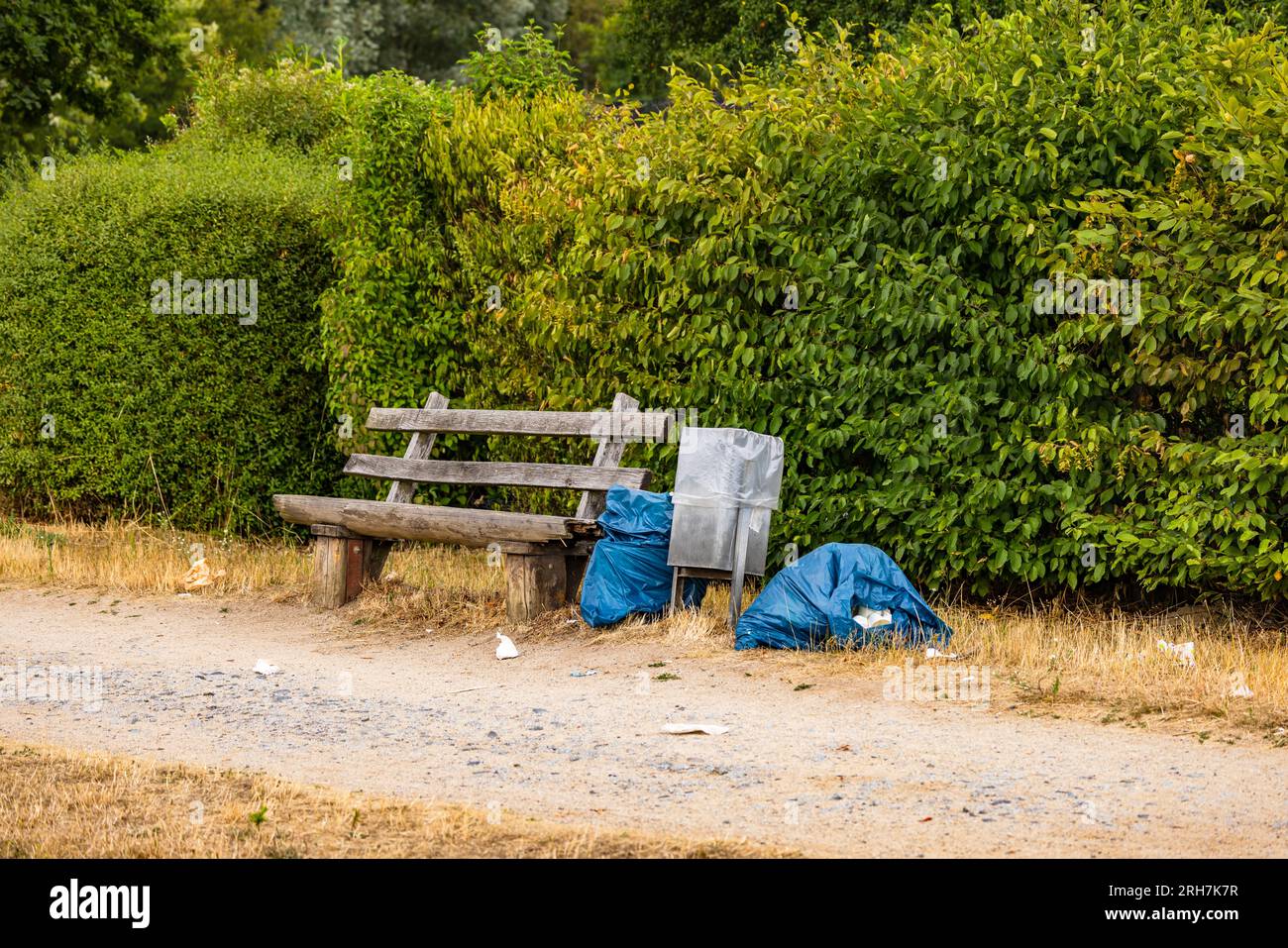 Trash and garbage in plastic bags next to a park bench with trash can ...
