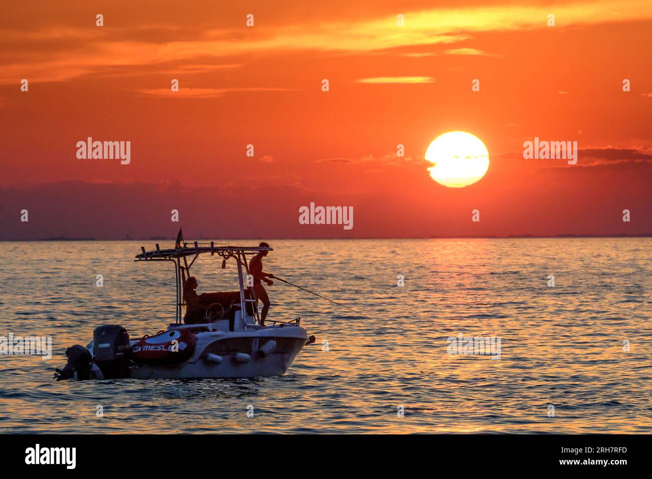 People fish from a boat as the sun sets over the Adriatic Sea off the ...