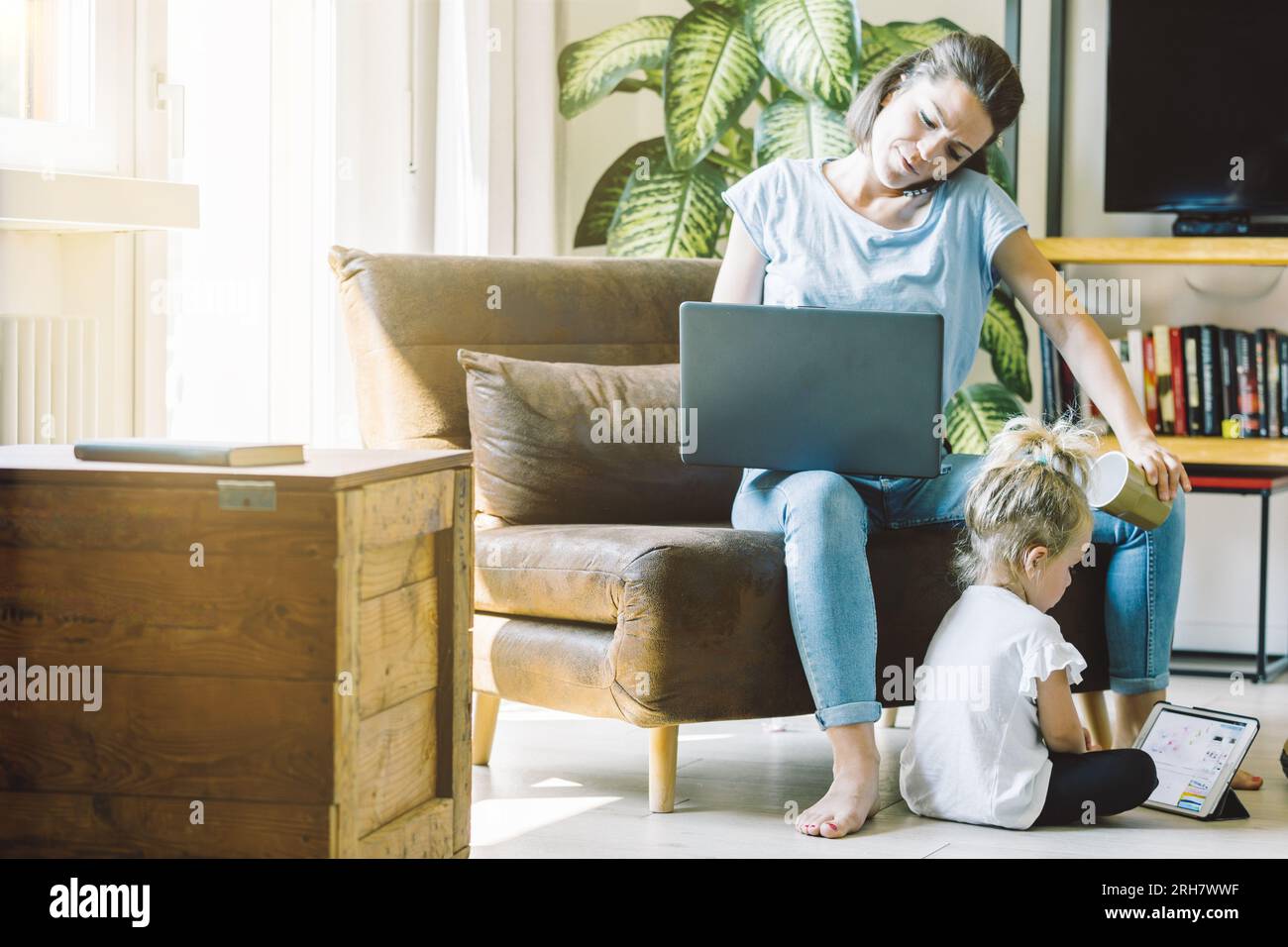 Little girl on tablet, mom on laptop in living room. Working, playing ...