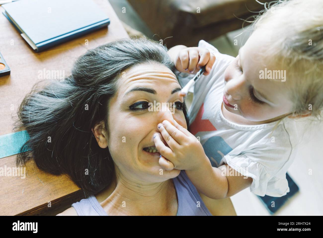 Mom and daughter play with makeup in the living room, laughing, feeling ...