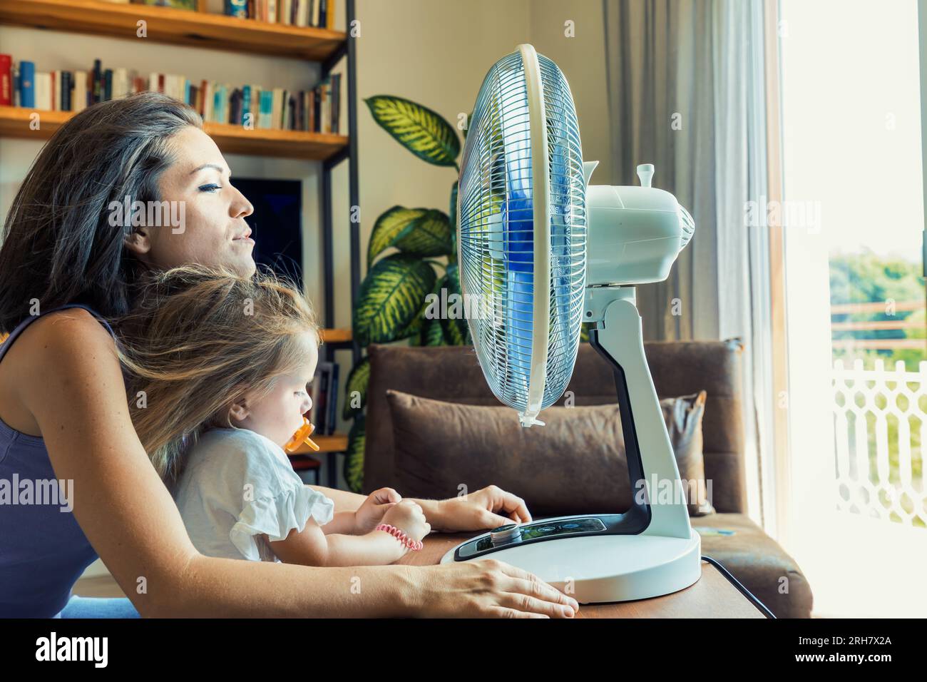 Mother and daughter make cooling off with a fan in the living room a ...