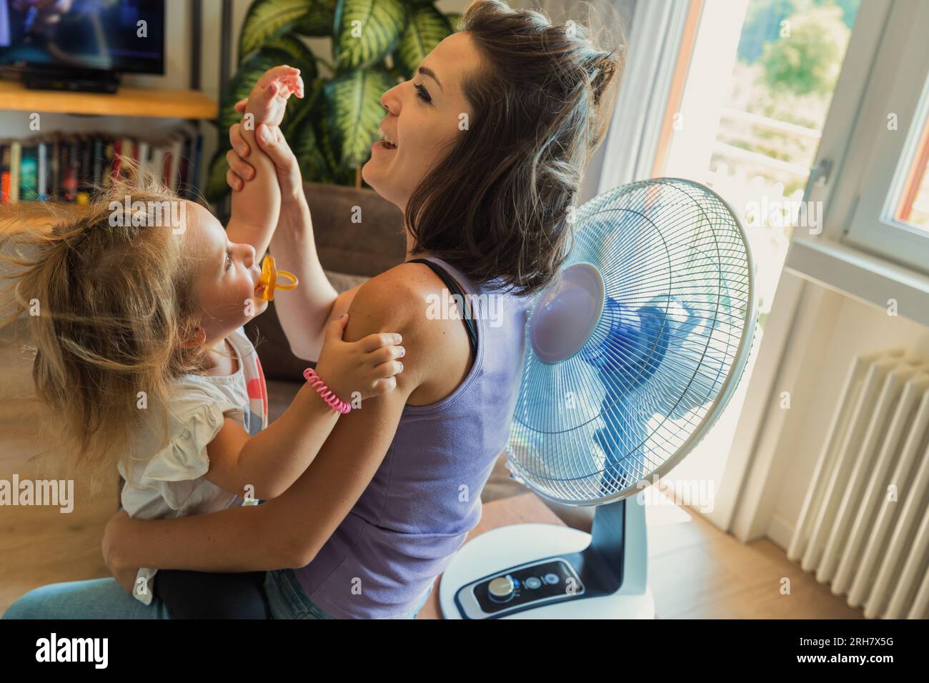 On a hot day, a mother and her young daughter turn the cooling fan into ...