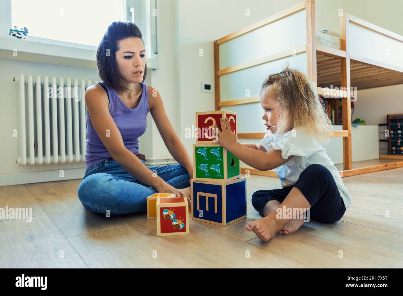 Bonding over wooden toys, a mother and her blonde daughter cherish ...