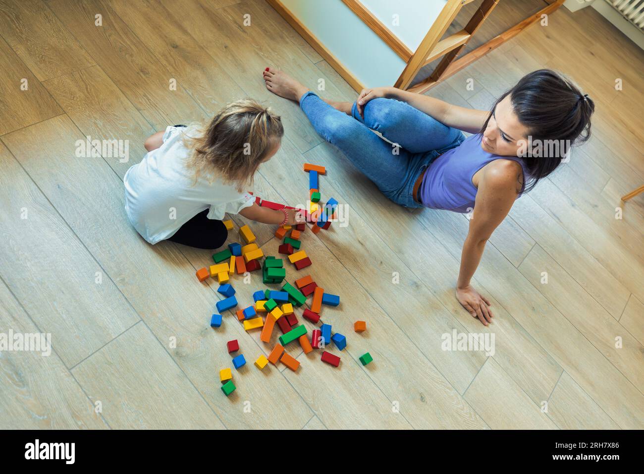Mom and daughter play in a room filled with wooden colorful toys, tables, blocks, enhancing ...