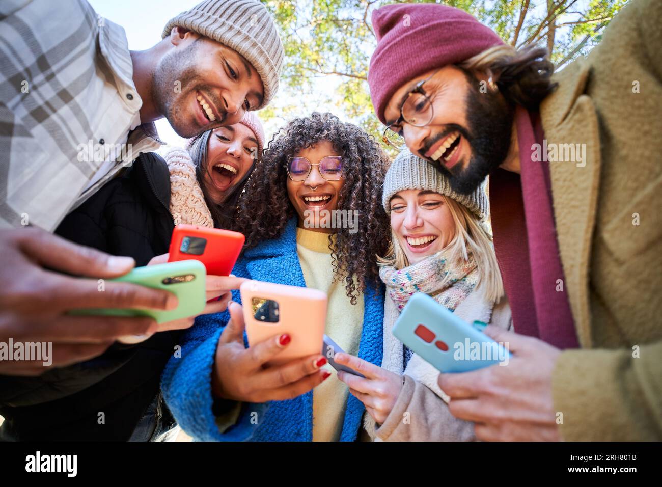 Group multiracial young people looking surprised at mobiles on winter ...