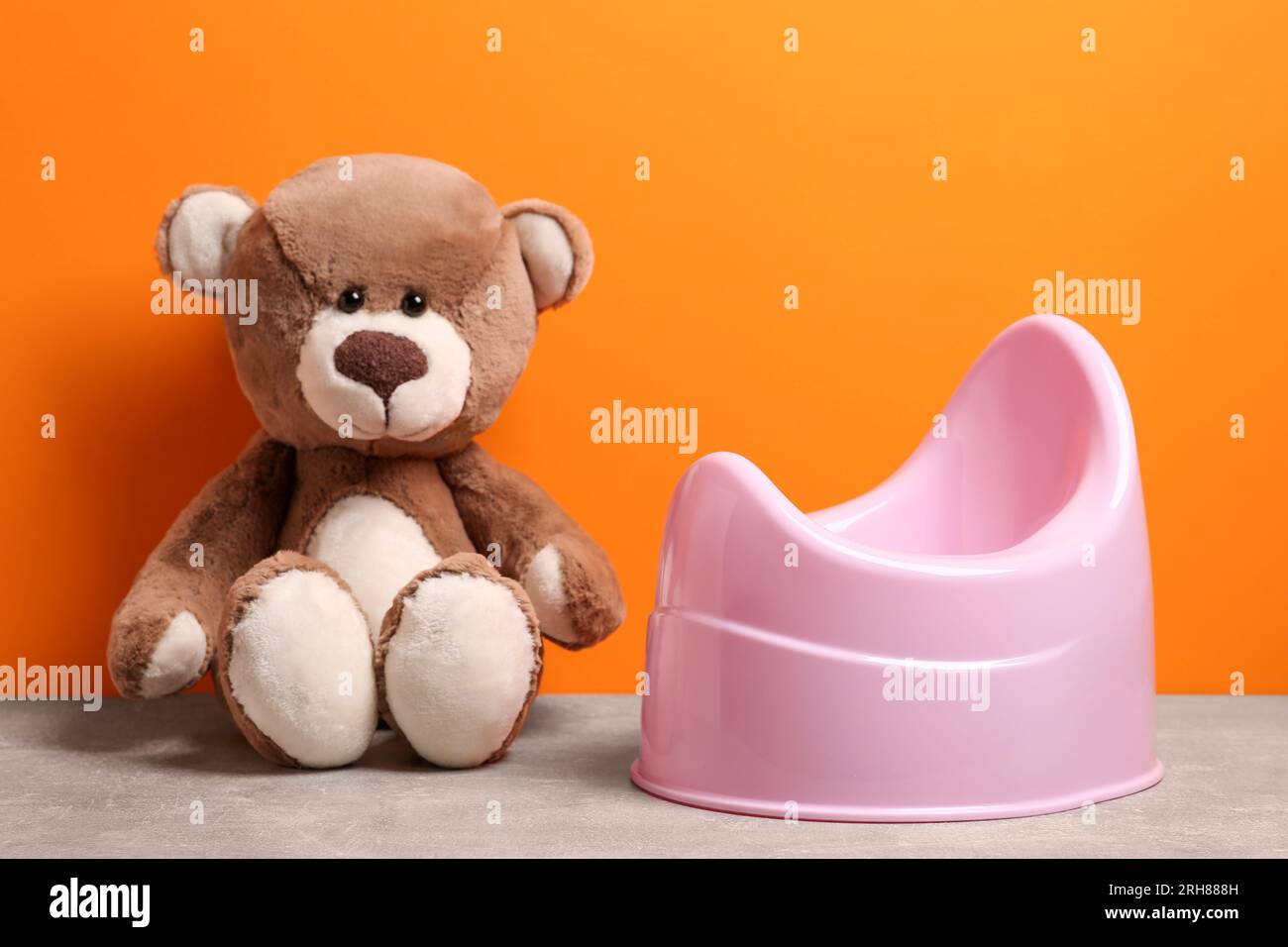 Teddy bear and pink baby potty on stone table against orange background ...