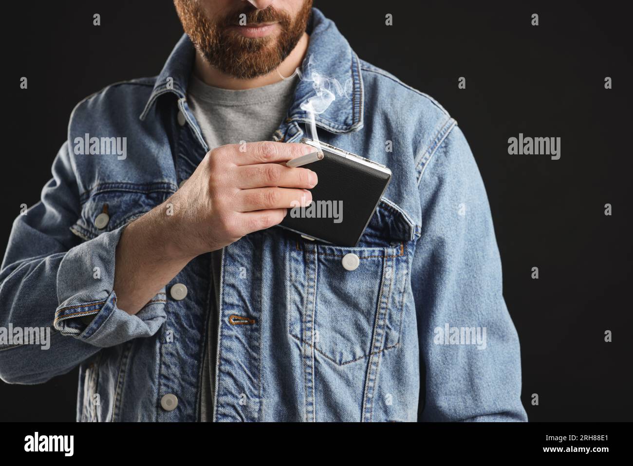 Man putting cigarette case into pocket on black background, closeup ...