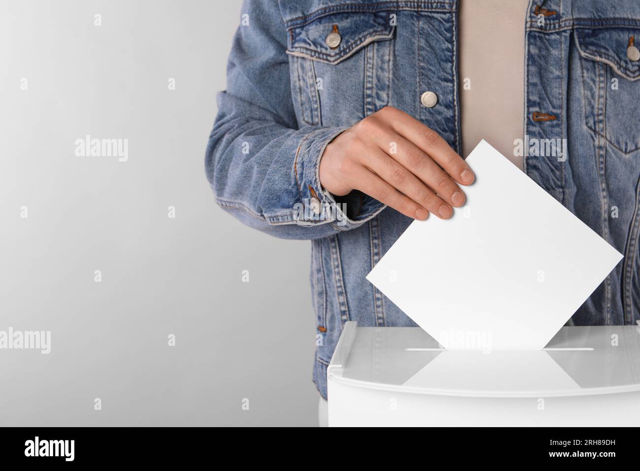 Man putting his vote into ballot box on light grey background, closeup ...