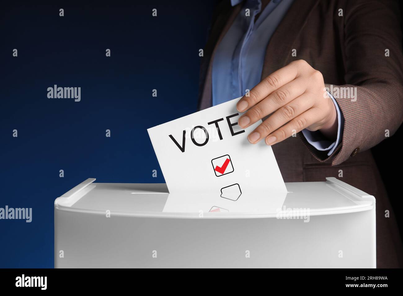 Woman putting paper with word Vote and tick into ballot box on dark ...
