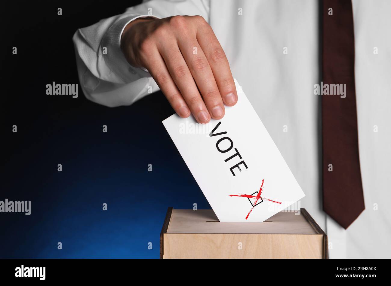 Man putting paper with word Vote and tick into ballot box on dark blue ...