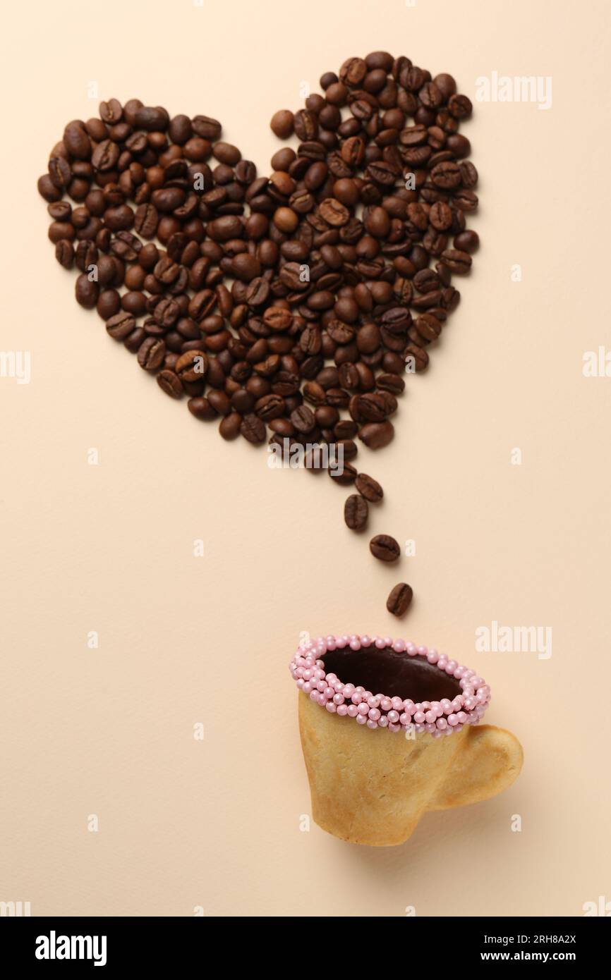 Coffee beans spilled from edible biscuit cup in shape of heart on beige ...