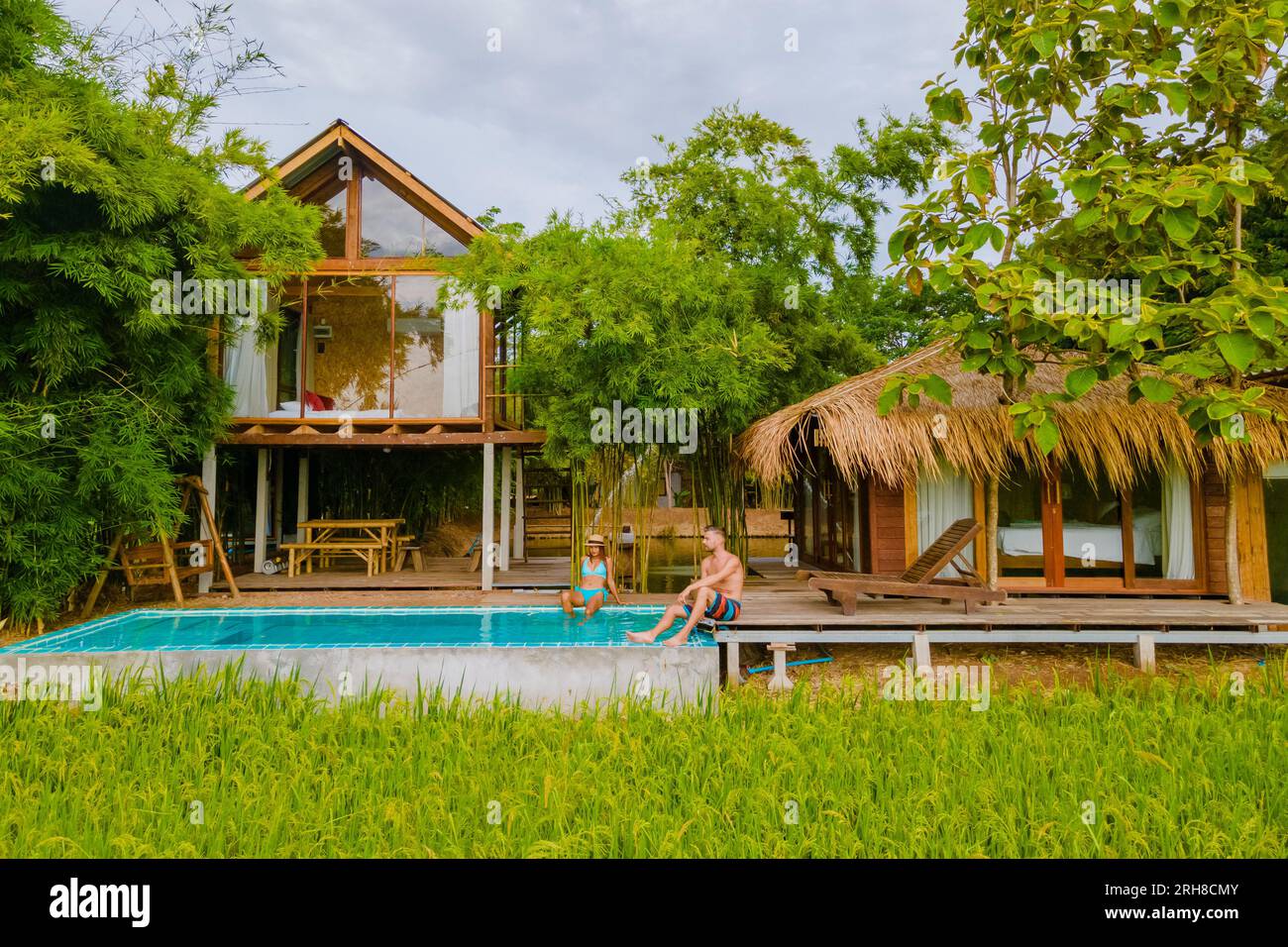 a couple of men and women in front of a Bamboo hut homestay farm, with ...