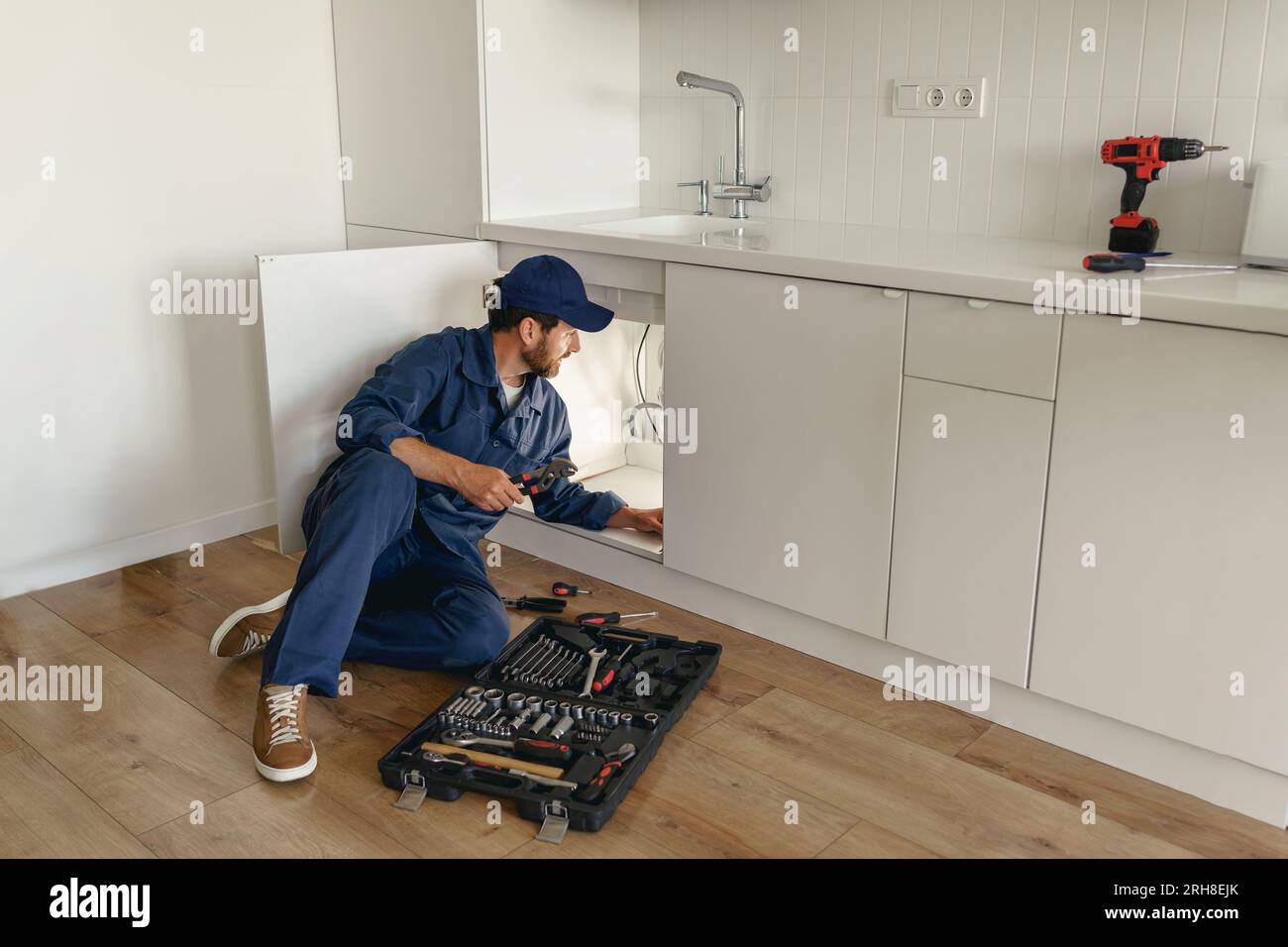 Professional plumber in blue uniform fixing broken water tap in kitchen ...