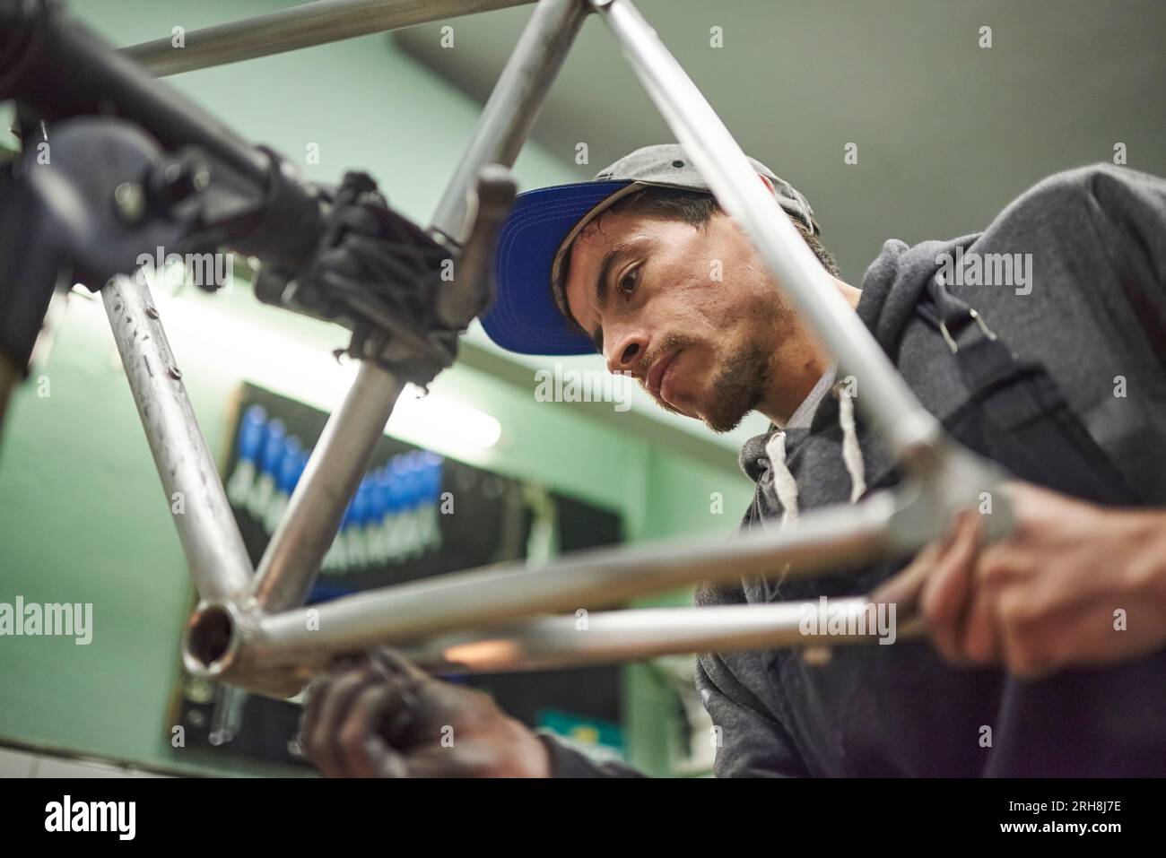 Hispanic man sanding an unpainted bicycle frame as part of the process ...