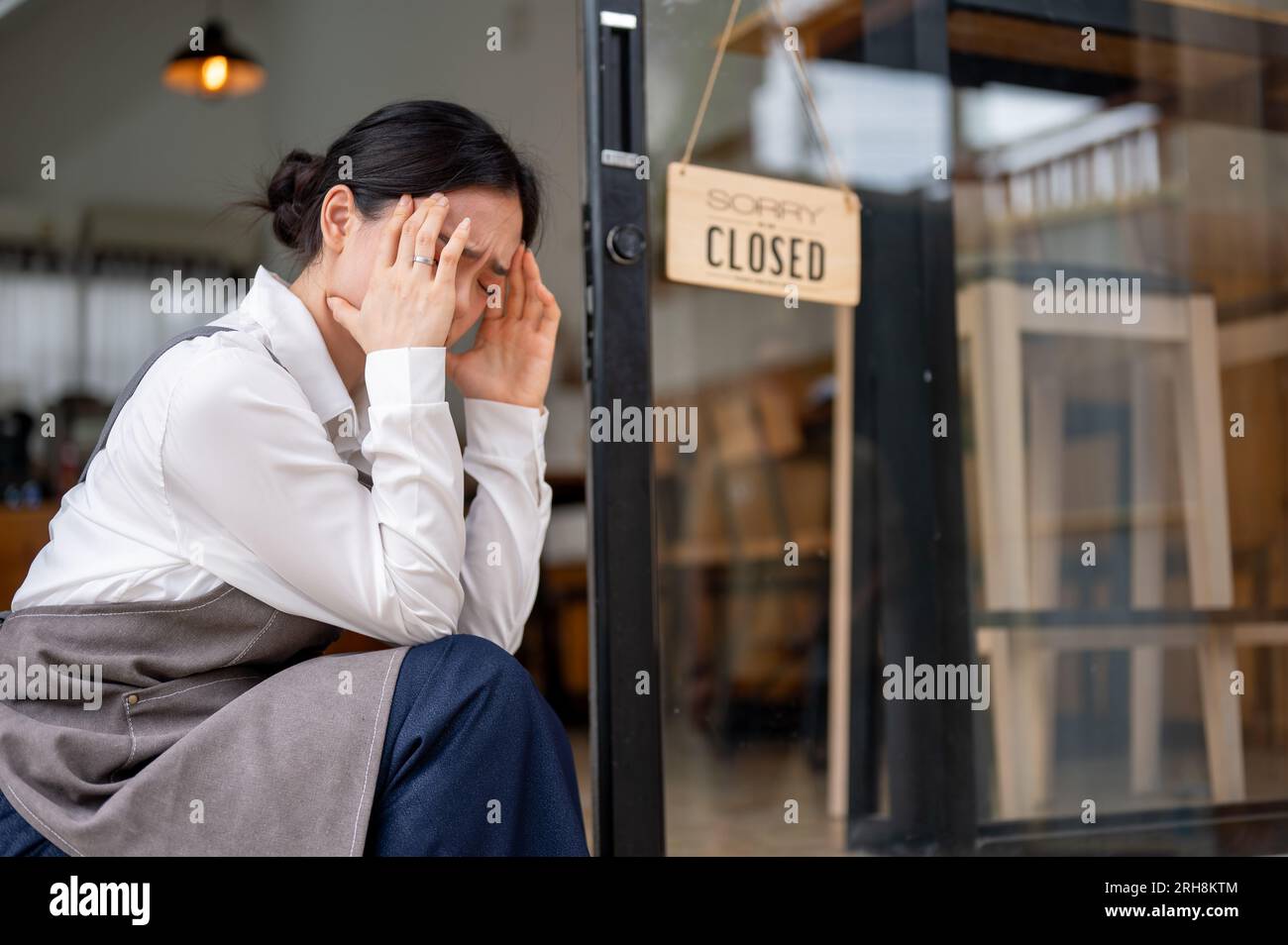 A crying and upset young Asian female coffee shop owner is hanging a ...