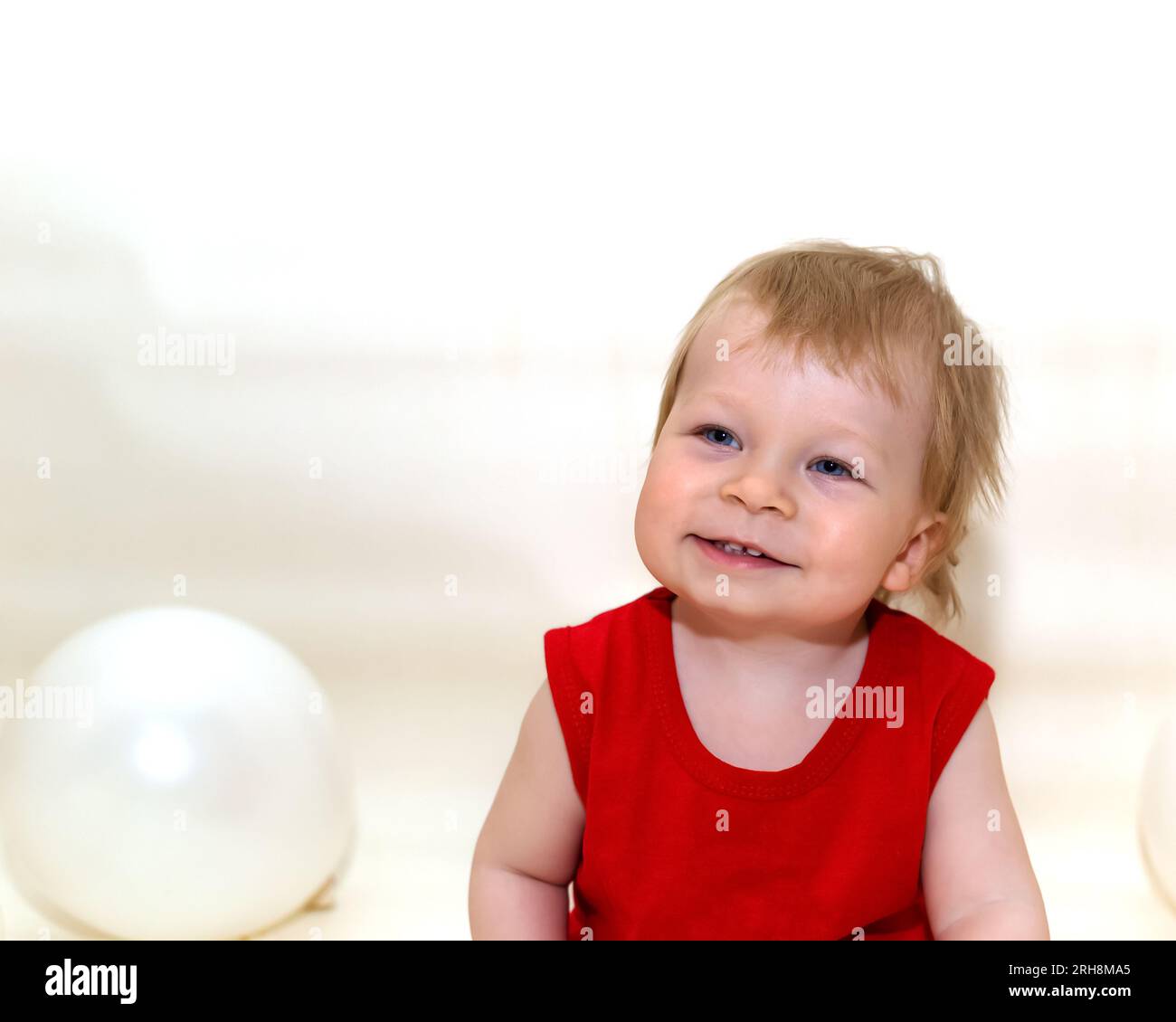 One-year-old toddler with blonde hair in red bodysuit sitting and ...