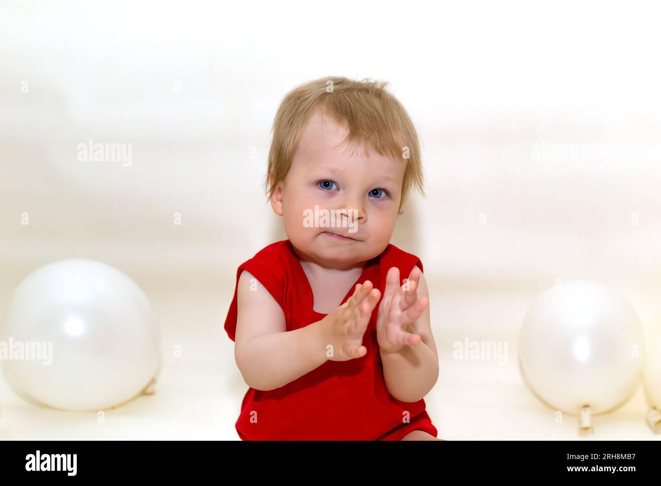 One-year-old toddler with blonde hair in red bodysuit sitting and ...
