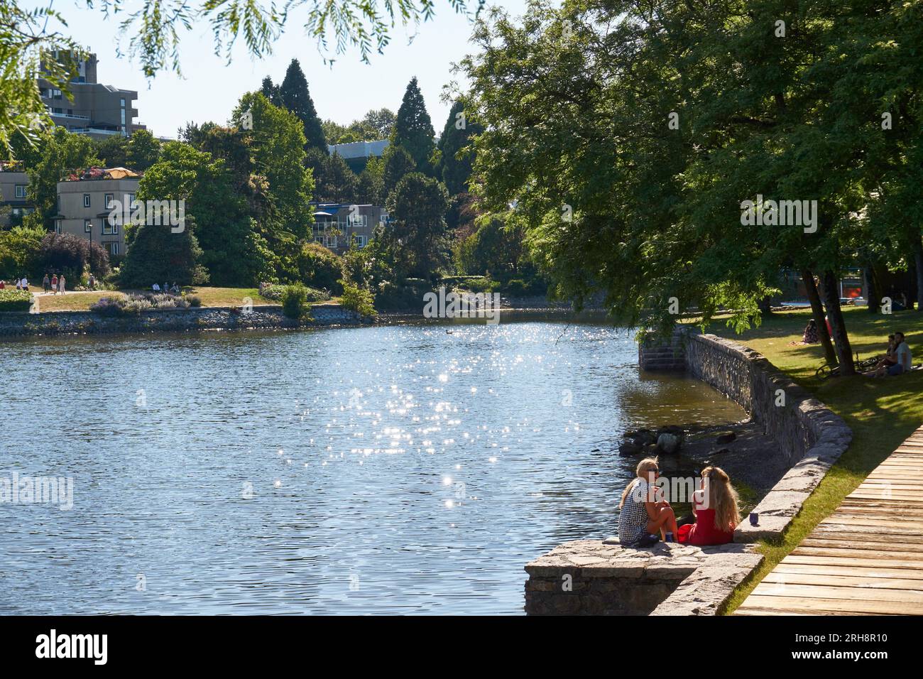 Two women sitting and chatting next to Alder Bay, Ron Basford Park, Granville Island, Vancouver ...