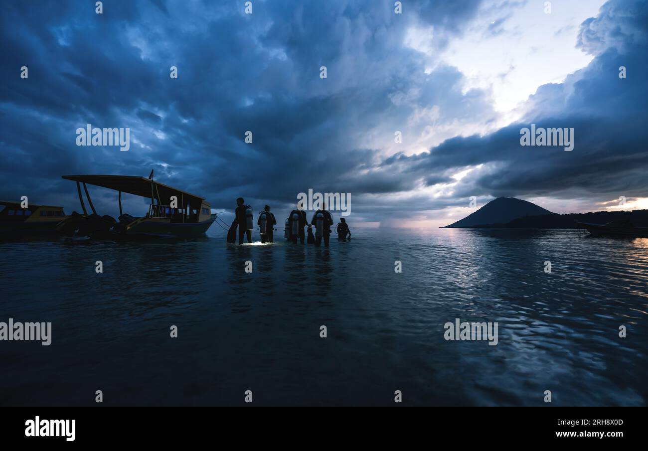 Divers walking into the ocean with tanks and torch during sunset for a ...