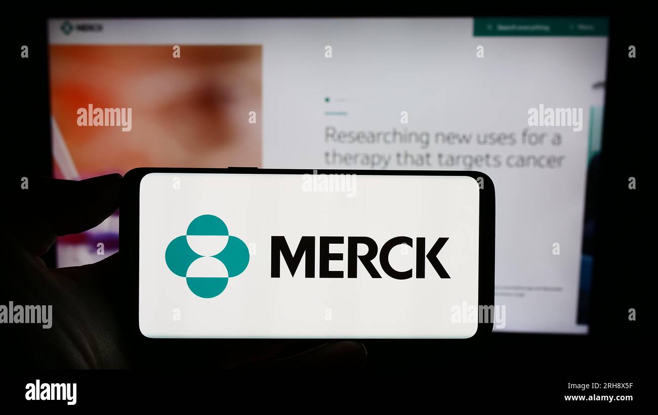 Person holding mobile phone with logo of American pharmaceutical company Merck Co. Inc. on ...