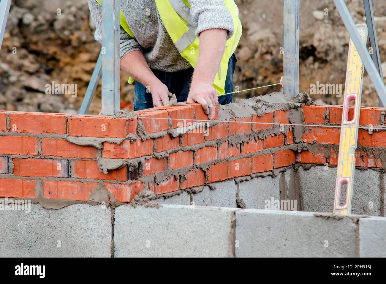 Hard working bricklayer lays bricks on cement mix on construction site ...