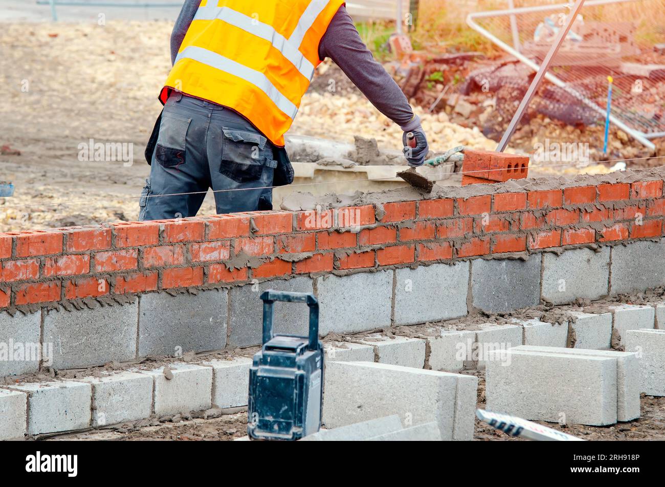 Hard working bricklayer lays bricks on cement mix on construction site ...