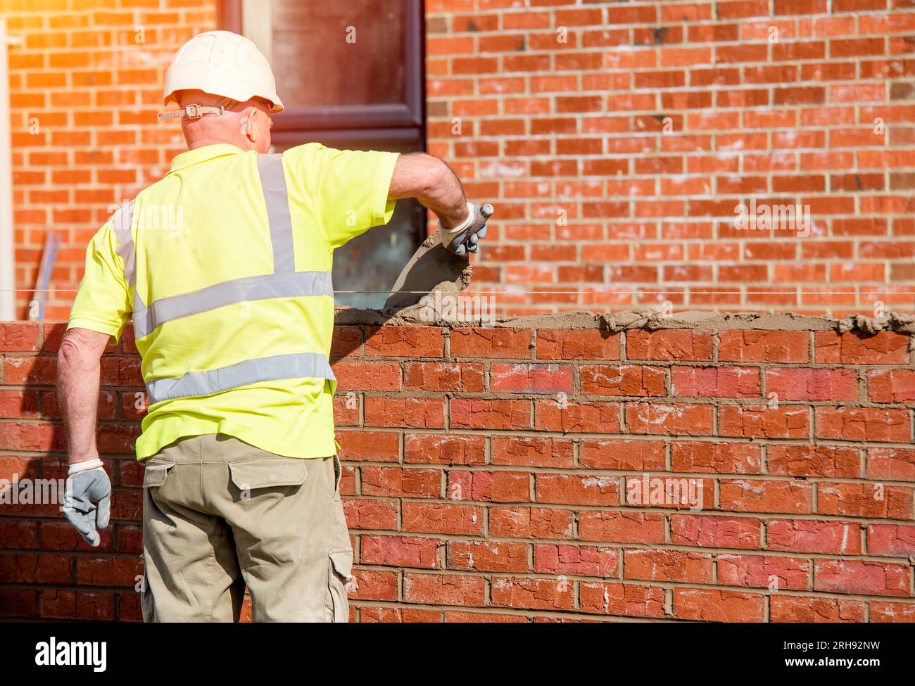 Hard working bricklayer lays bricks on cement mix on construction site ...