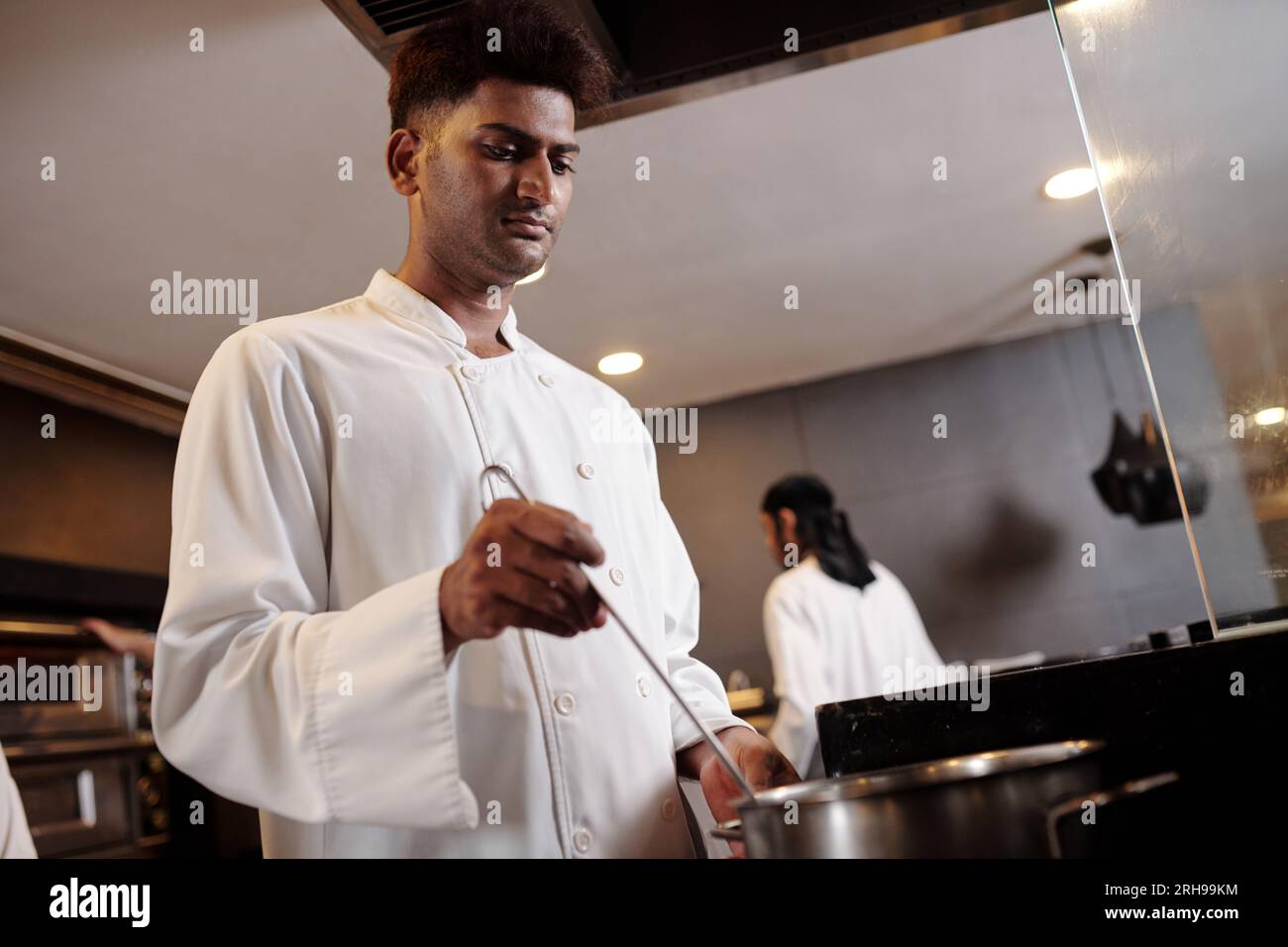 Serious chef in white uniform mixing soup in big saucepan Stock Photo ...