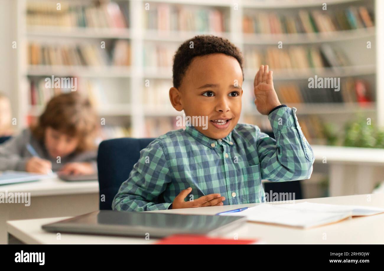 Smart black boy raising his hand to answer a question during lesson in ...