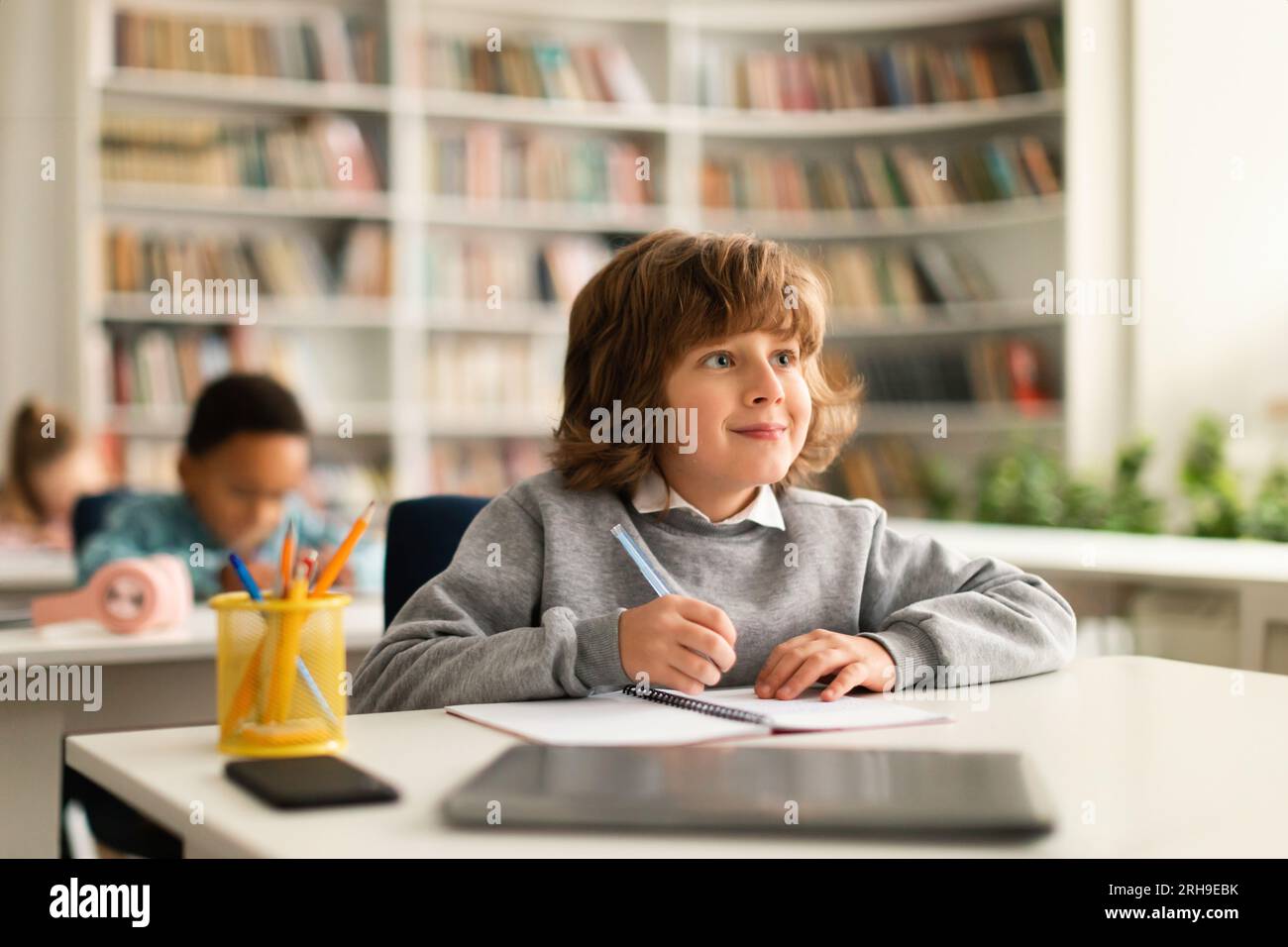 First day at school. Smiling diligent boy sitting at table in classroom ...