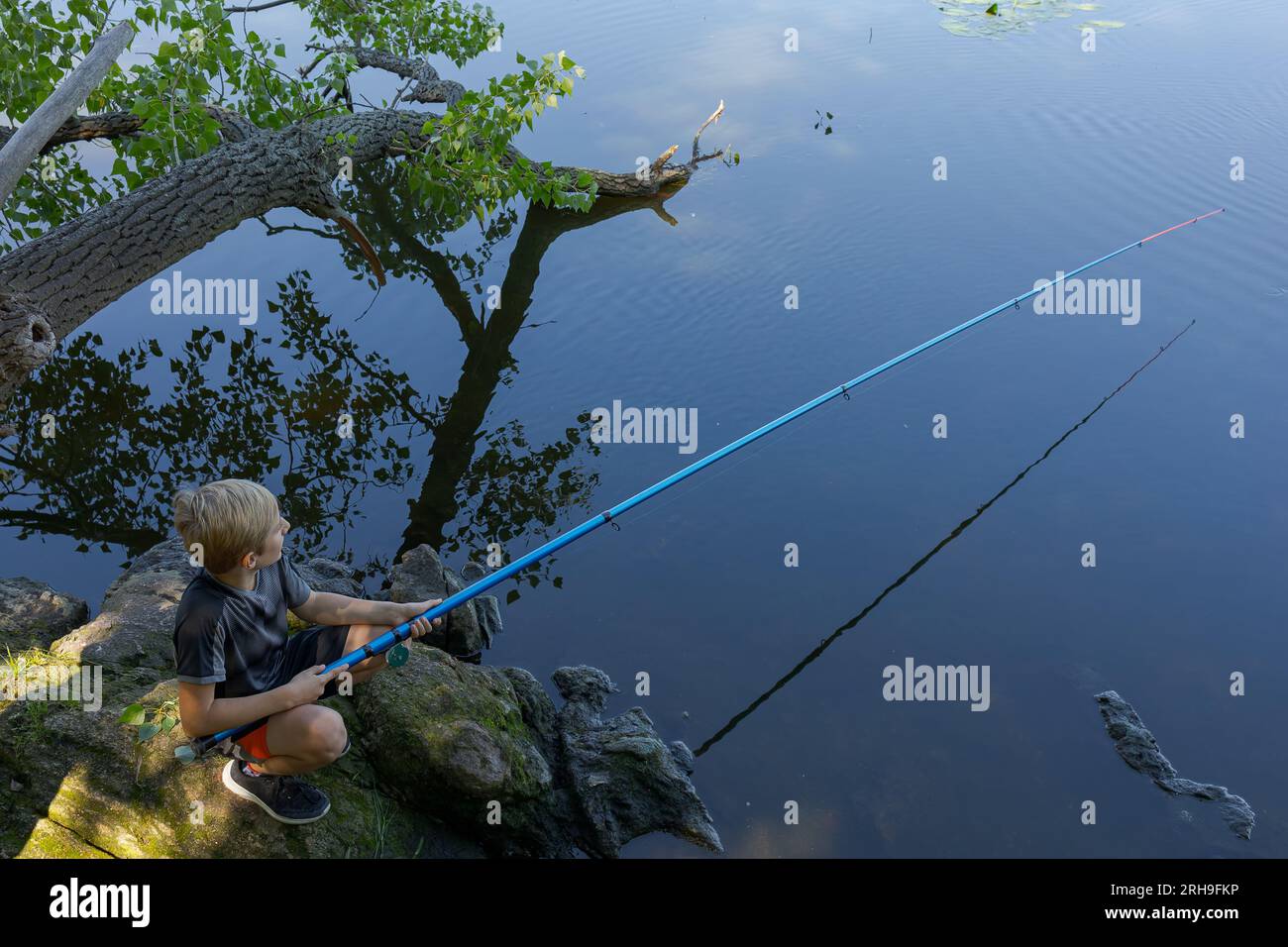 A boy squats on rocks and catches fish. Sport fishing on the river in ...