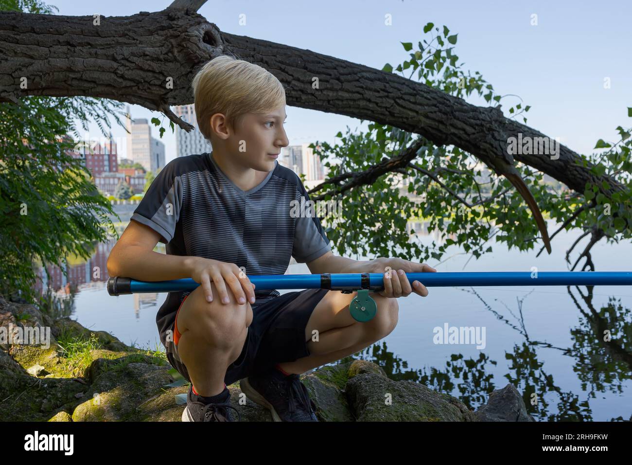 A boy squats on rocks and catches fish. Sport fishing on the river in ...