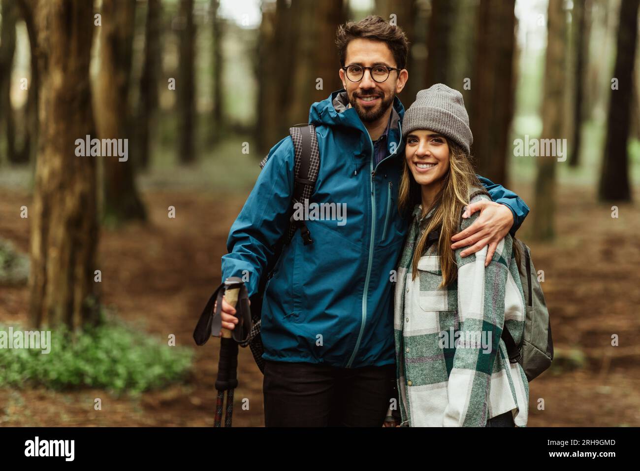 Positive young caucasian couple in jackets with trekking sticks walk in ...