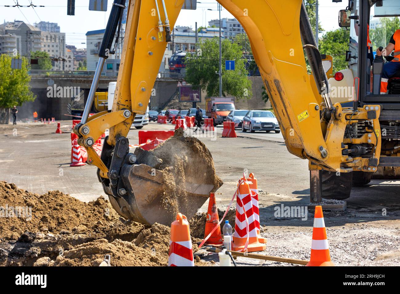 The bucket of a construction excavator digs a trench on the road ...