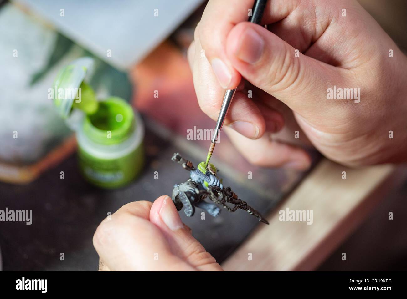Close up of a man painting a Warhammer Squig Hog Boy with green paint ...