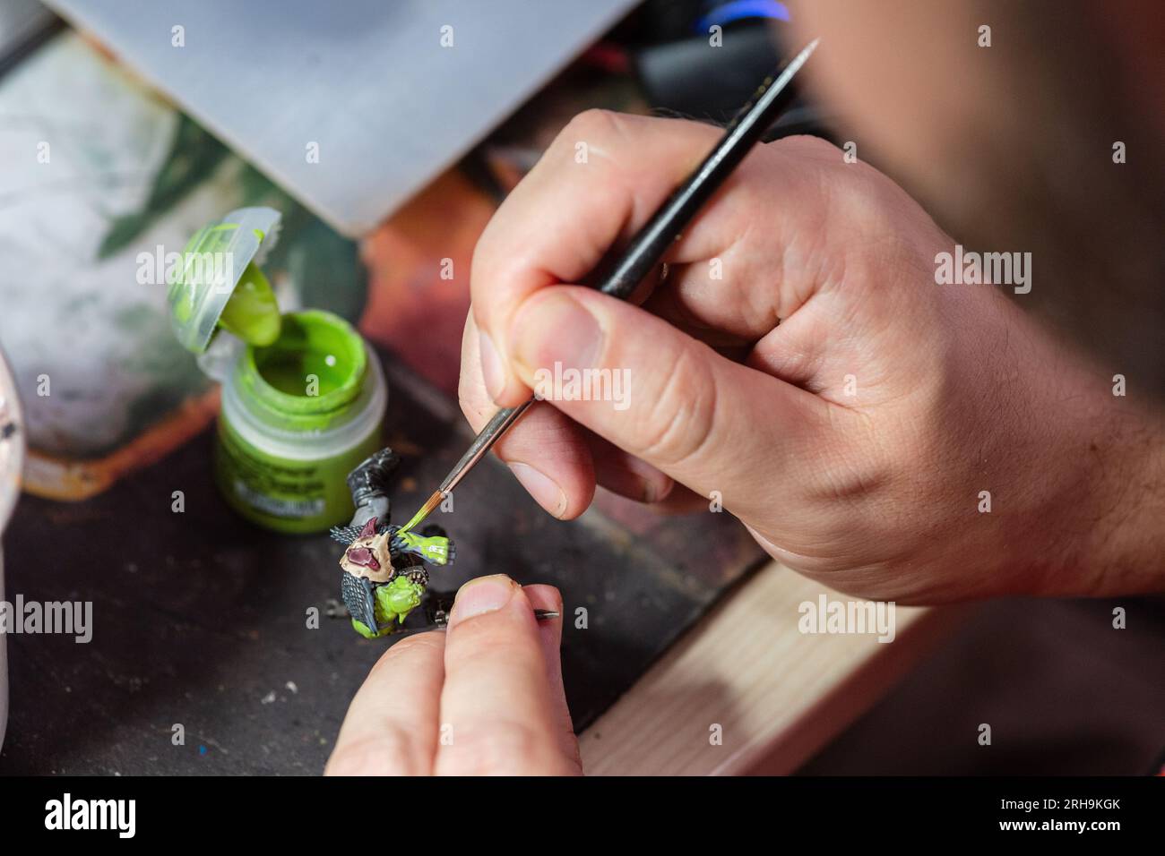 Close up of a man painting a Warhammer Squig Hog Boy with green paint ...