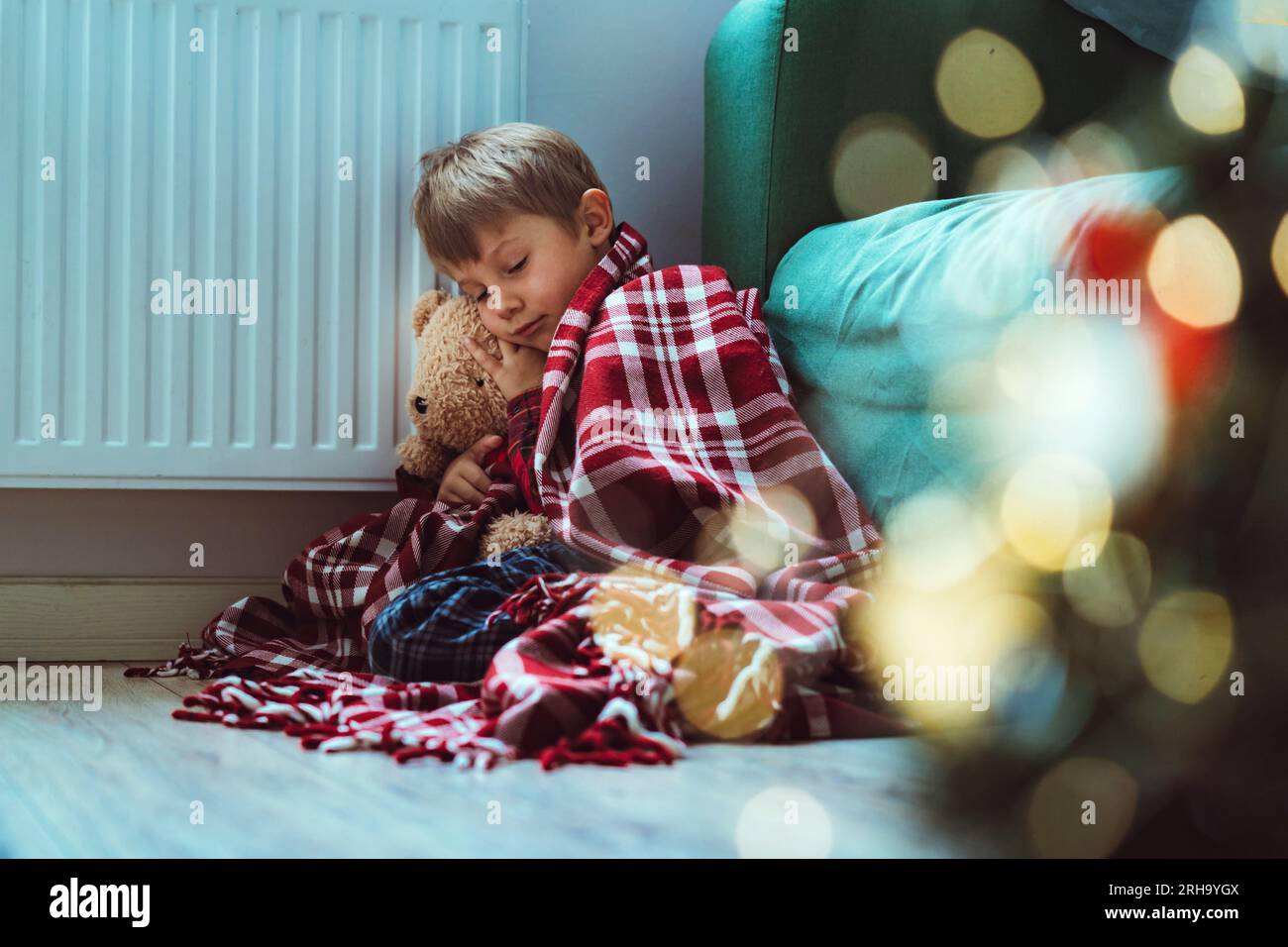 cute little boy wrapped id plaid falling asleep by heater hugging teddy ...
