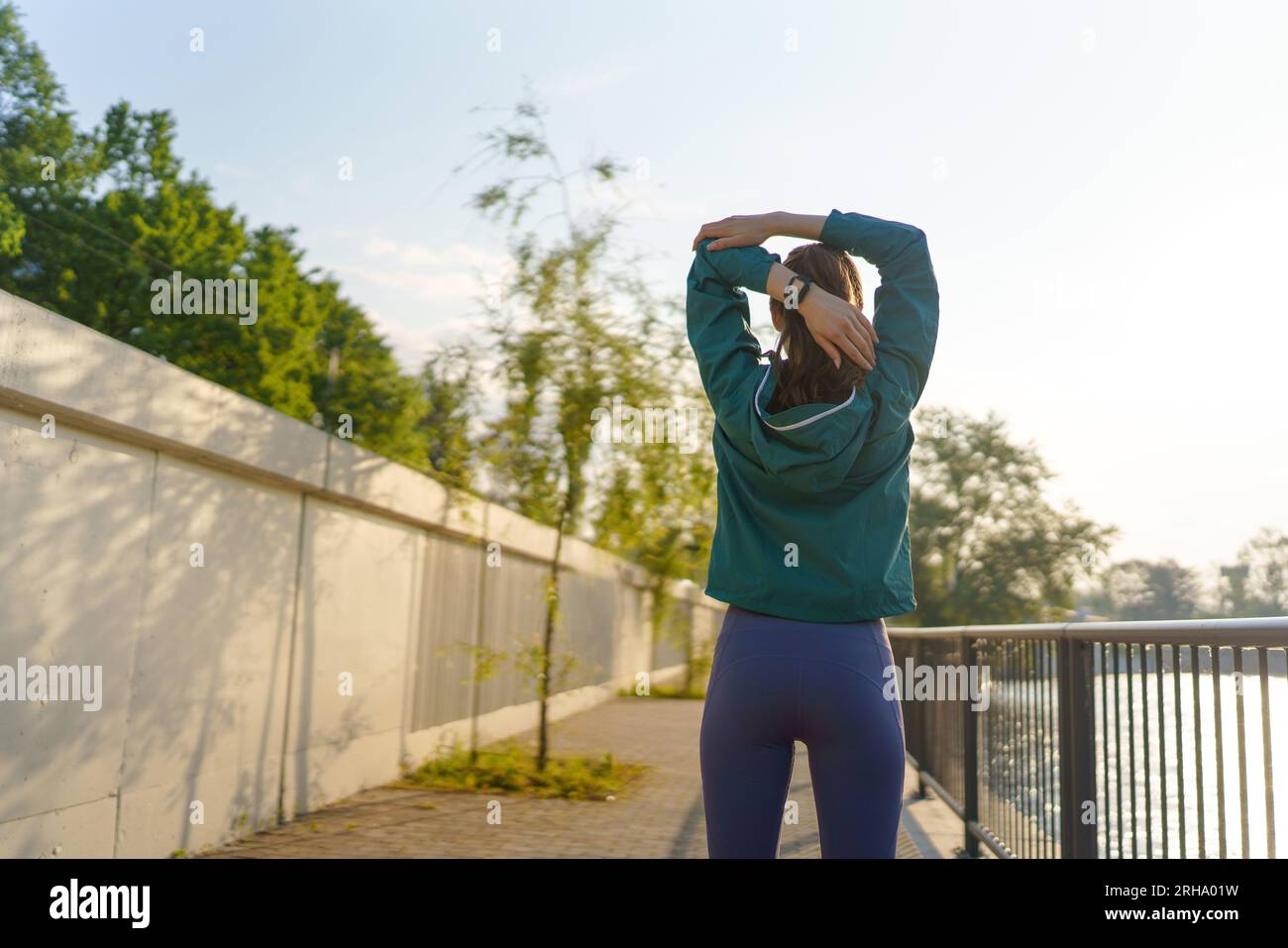 Rear view of attractive female runner stretching her arms before her ...