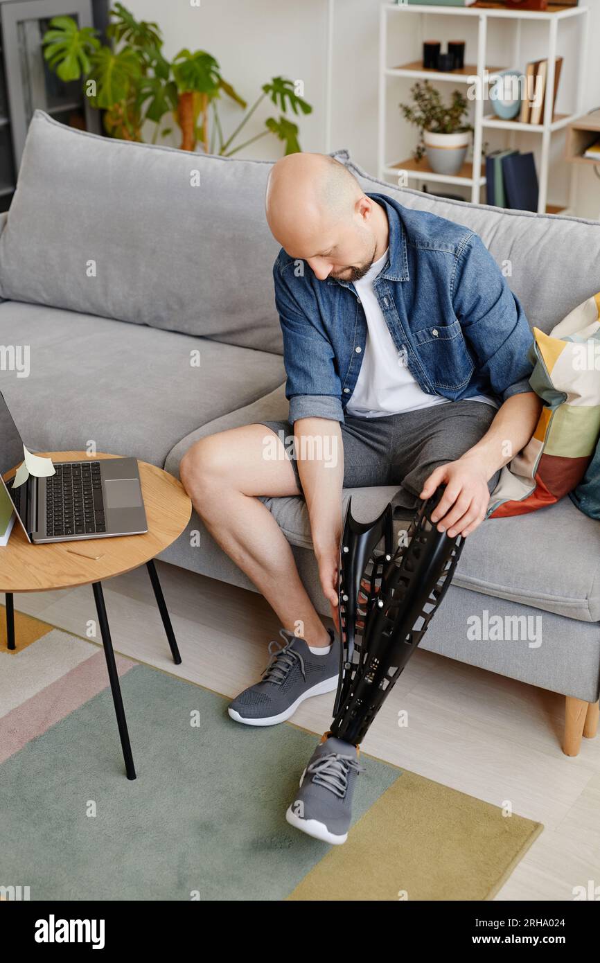 Vertical full length portrait of adult man putting on prosthetic leg at ...