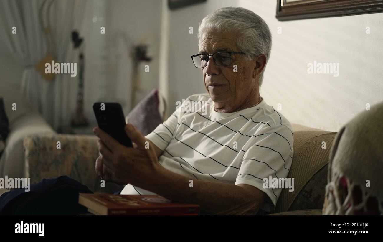 Elderly man staring at cellphone device sitting at home couch with ...