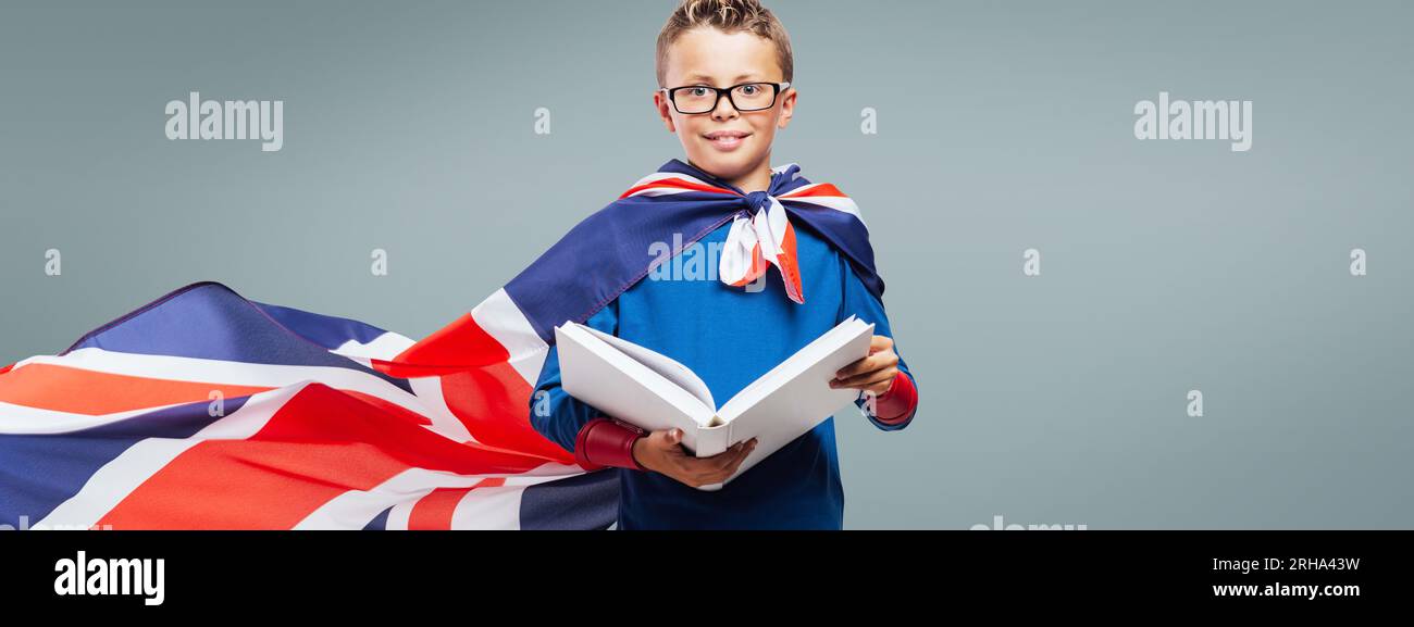 Cute superhero boy reading a book, he is wearing a British flag as a ...
